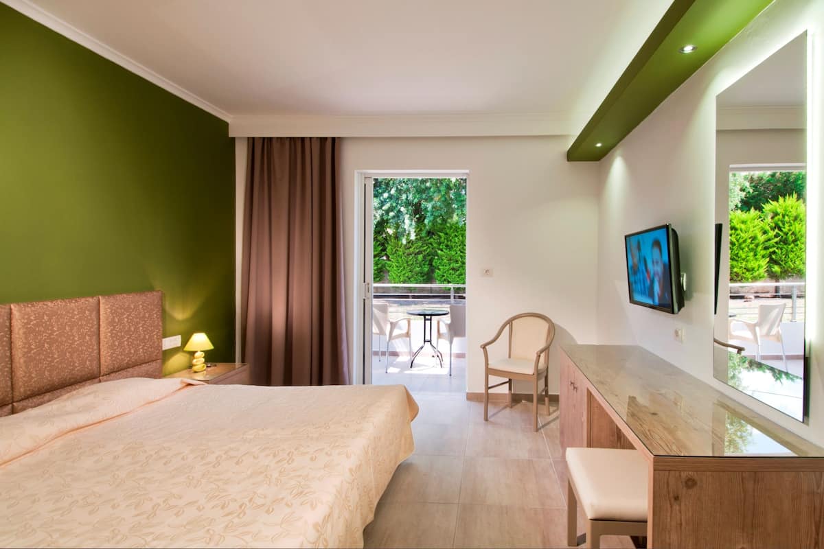 Quarto de hotel com cama, escrivaninha, cadeira, televisão e varanda com mobiliário.