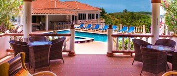 Área à beira da piscina com espreguiçadeiras, um bar e vista para a piscina.