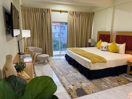 Quarto de hotel com cama, escrivaninha, poltrona, televisão e vista para o exterior.