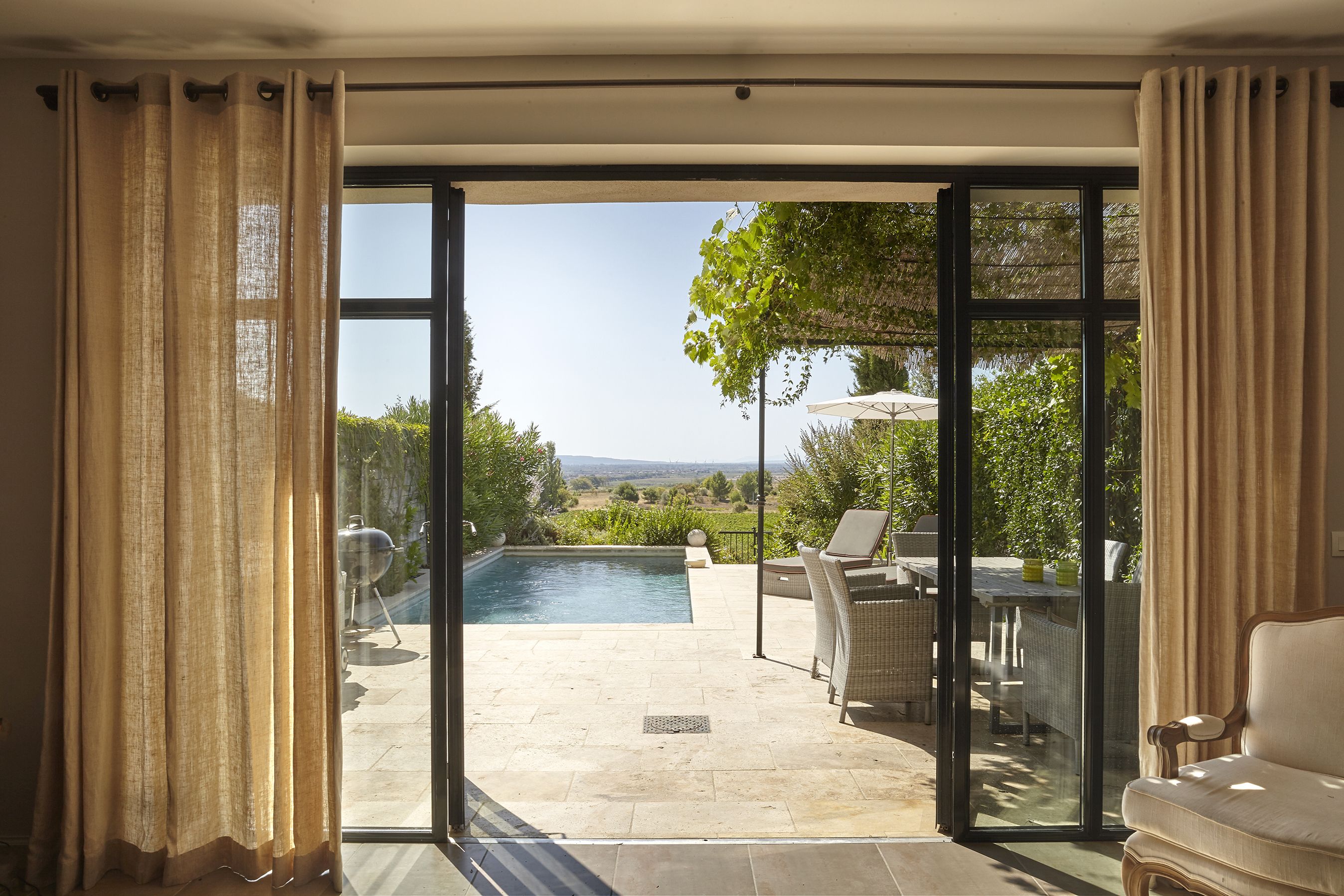 Quarto com uma grande porta de correr de vidro que dá para área externa com piscina, móveis de pátio e vista para vegetação e colinas.