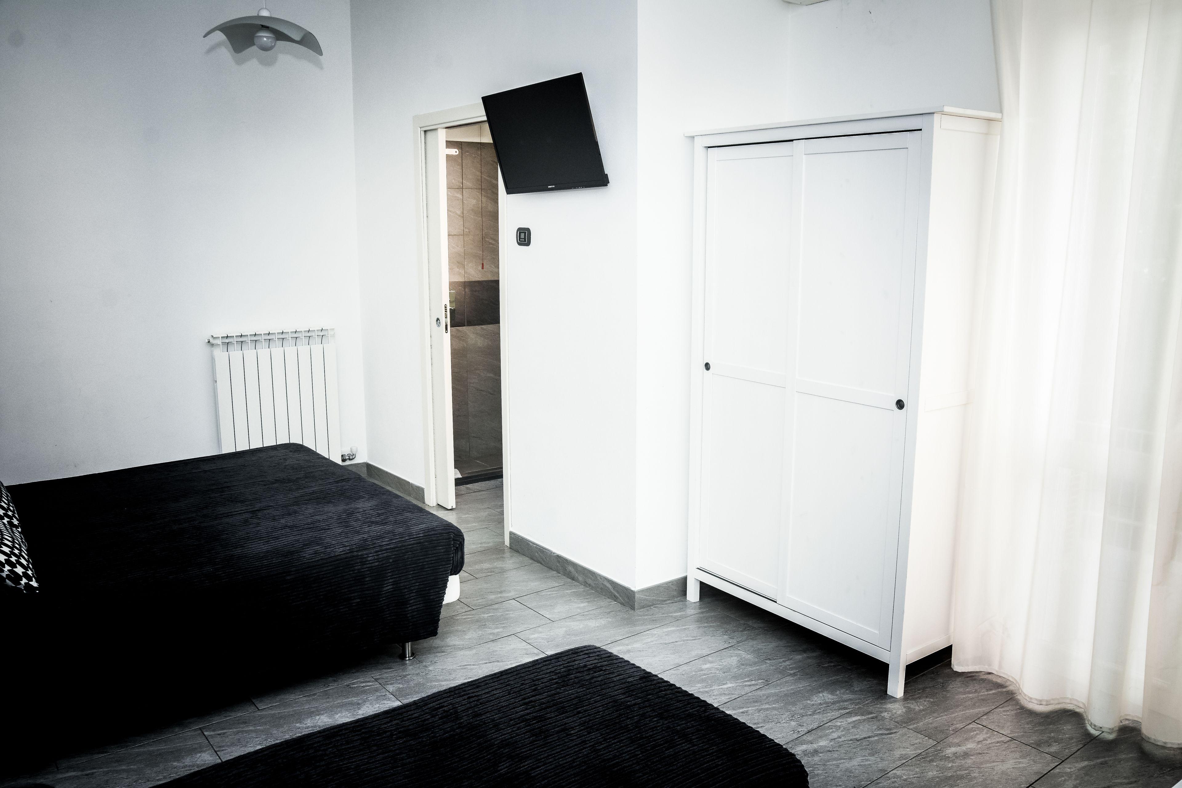 Quarto com cama, guarda-roupa, televisão e banheiro visível por uma porta aberta.