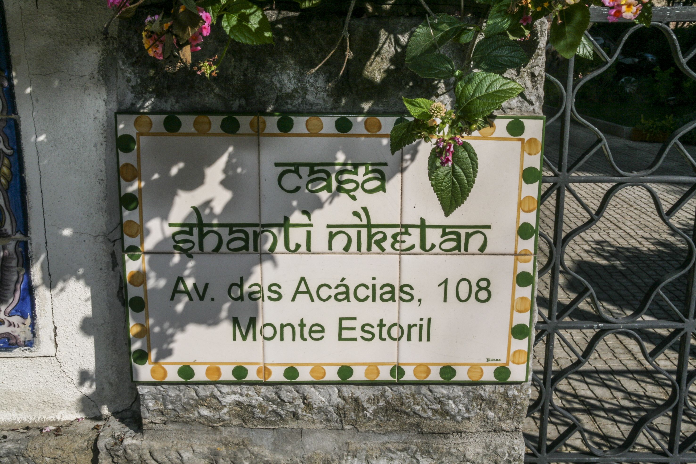 Placa com o texto 'casa shanti niketan' e endereço 'Av. das Acácias, 108 Monte Estoril'.