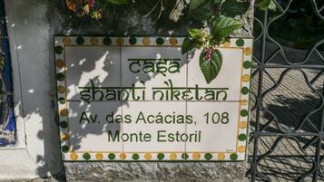 Placa com o texto 'casa shanti niketan' e endereço 'Av. das Acácias, 108 Monte Estoril'.