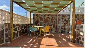 Um pátio com pérgola de madeira, paredes de pedra e piso de azulejos.