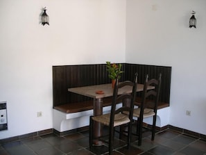 Uma área de refeições no canto com uma mesa e cadeiras de madeira, uma pequena planta em vaso e duas lanternas fixadas na parede.
