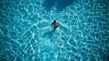 Uma pessoa nadando em uma piscina com água azul cristalina e ondulações visíveis.