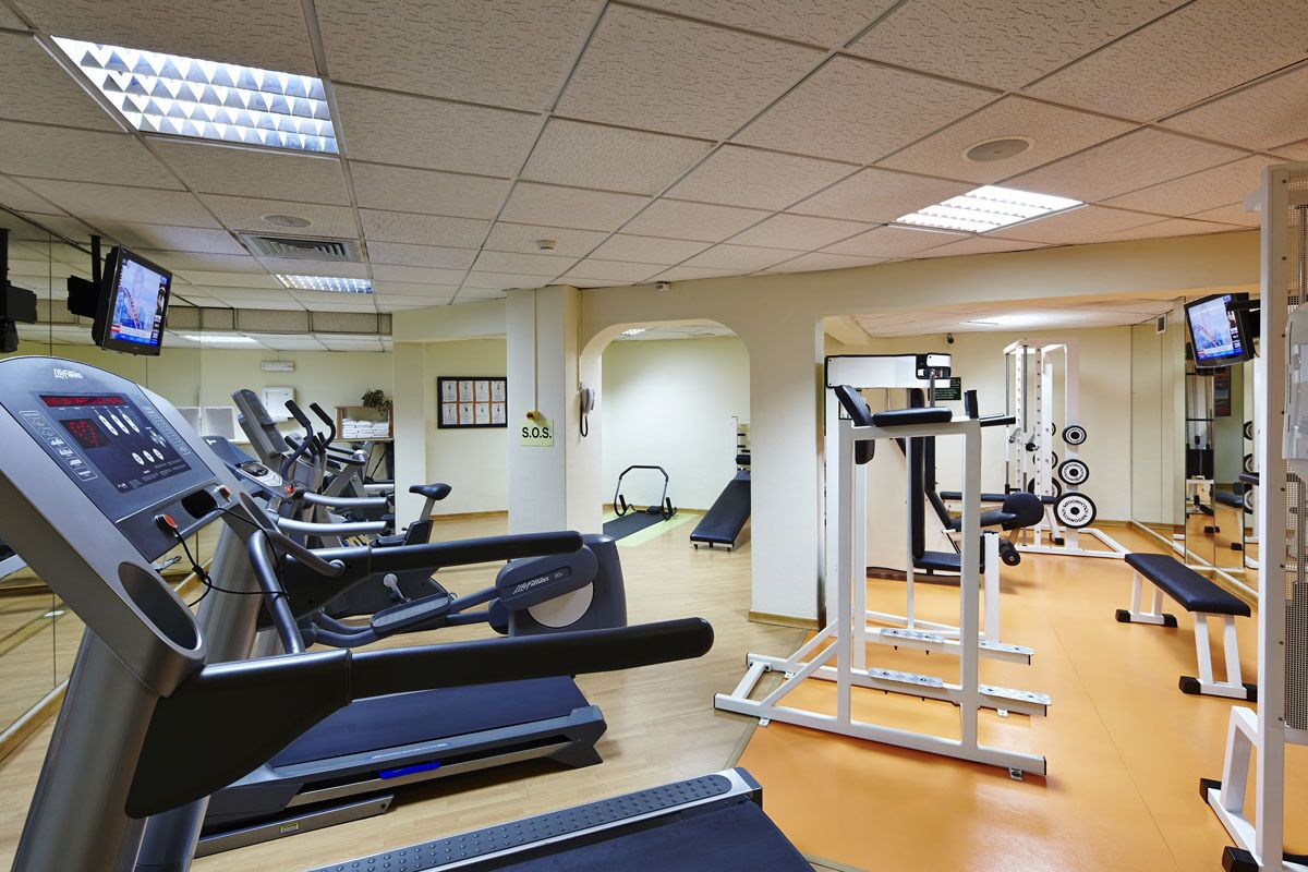 Uma academia com esteiras, máquinas de musculação e colchonetes.