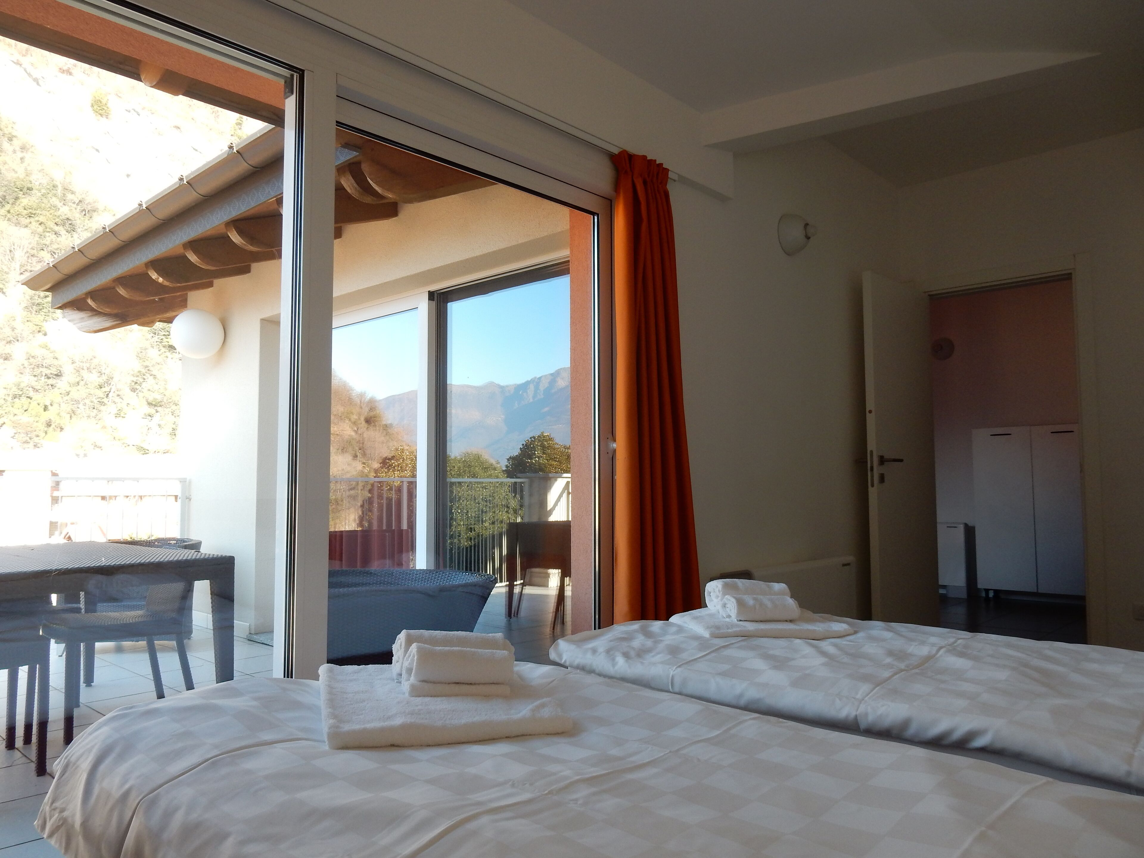 Quarto de hotel com duas camas, uma mesa de jantar e vista para montanhas através de uma grande janela.