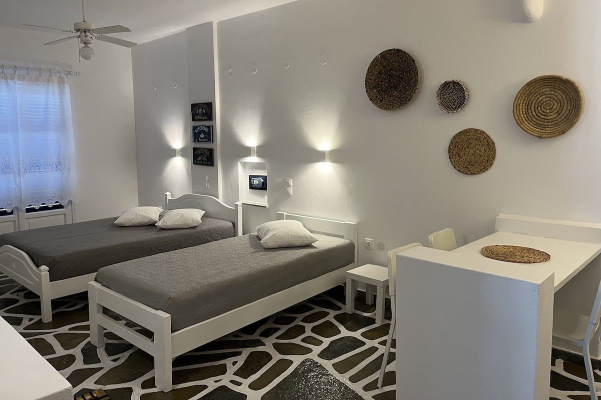 Quarto com duas camas, uma escrivaninha, uma cadeira, ventoinha no teto e luminárias fixadas na parede.