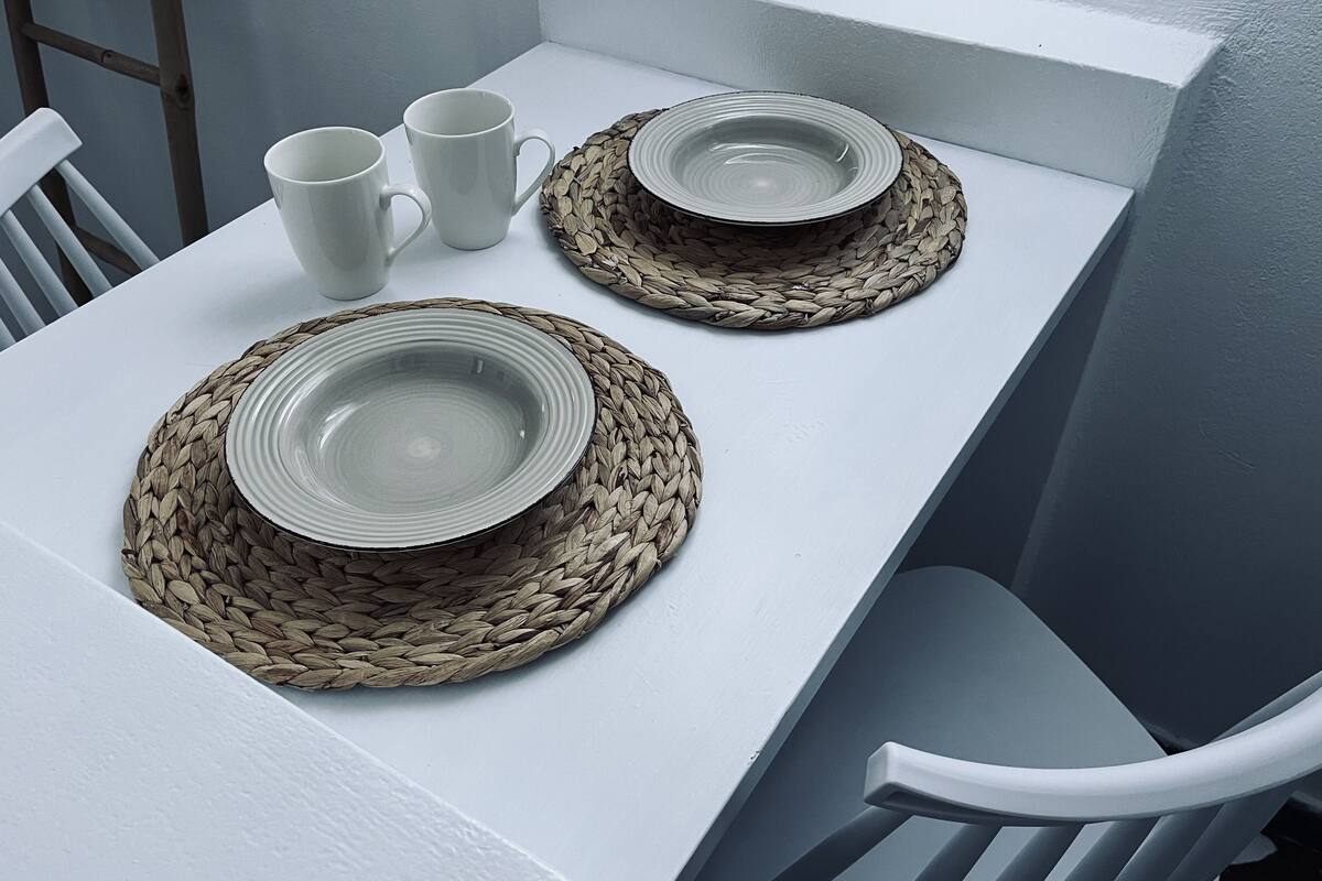 Mesa branca com dois individuais de tecido trançado e duas travessas de cerâmica branca.