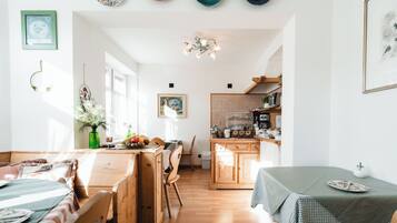 Cozinha iluminada com armários de madeira, área de refeições com um banco e uma mesa com toalha verde.