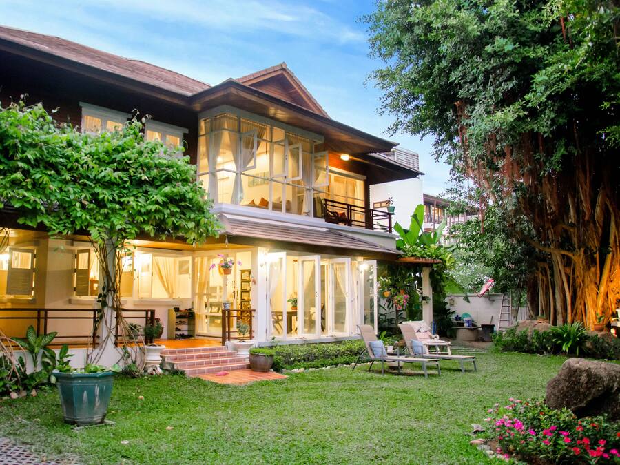 Uma casa de dois andares com fachada envidraçada generosa, varanda e um jardim bem cuidado com uma árvore e plantas em vasos.