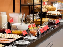 Buffet com diversos alimentos e acompanhamentos, incluindo iogurte, queijo e pastas.