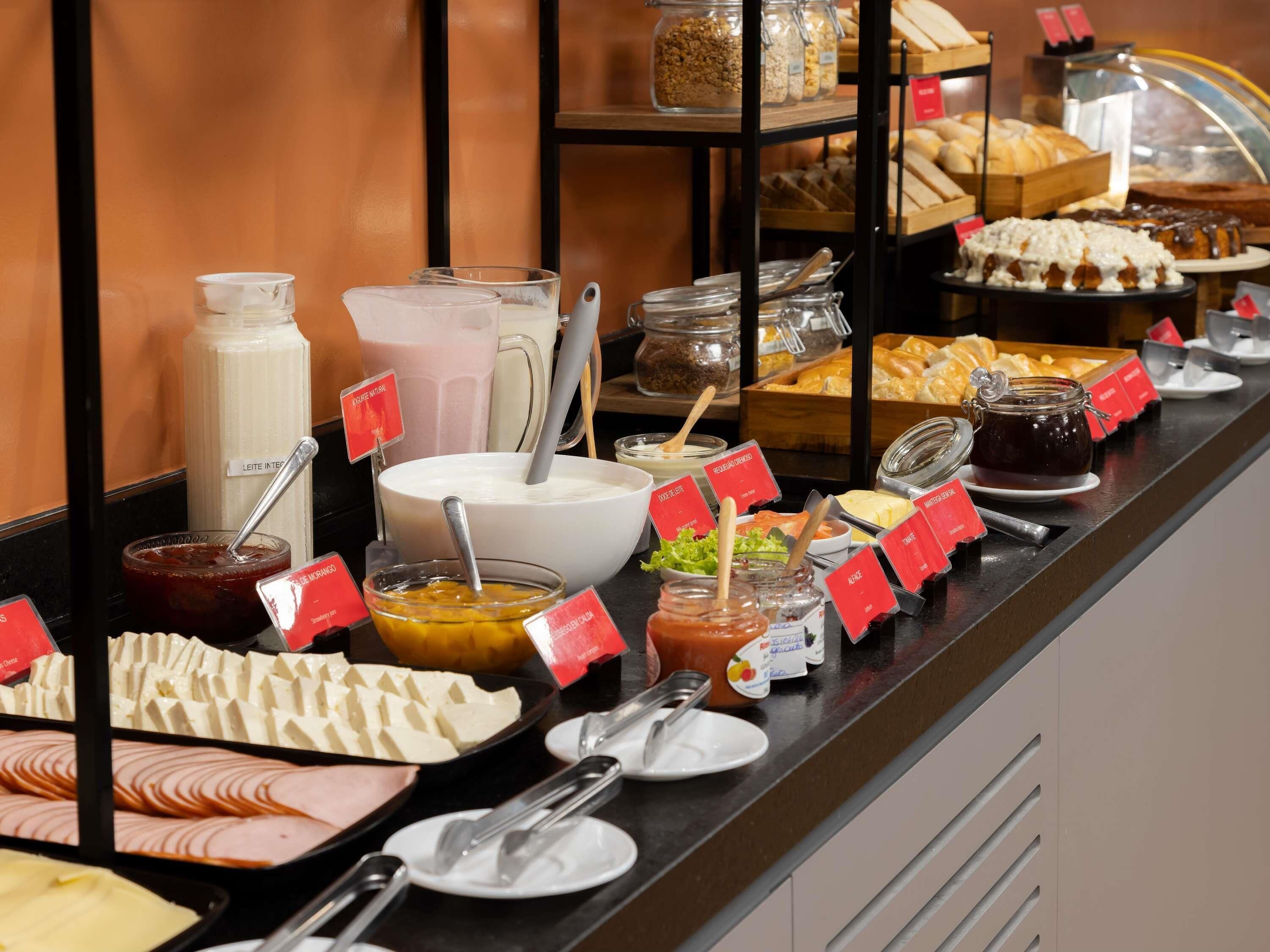 Buffet com diversos alimentos e acompanhamentos, incluindo carnes fatiadas, queijos e patês.