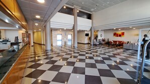 Um hall amplo com piso xadrez, balcão de recepção, área de estar e escada que leva a um andar superior.