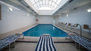 Piscina interna com claraboia, cadeiras de descanso e cadeira do salva-vidas.