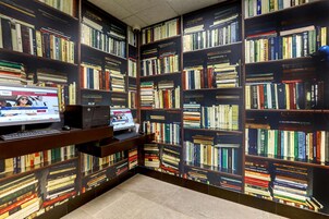 Uma biblioteca com estantes cheias de livros, um computador e uma mesa com teclado e rato.