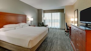 Quarto de hotel com uma cama grande, uma escrivaninha, uma cadeira, uma televisão e um armário.