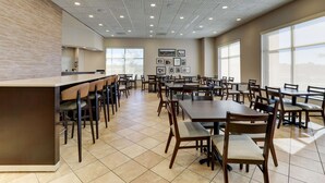 Uma sala de jantar ampla com várias mesas e cadeiras, um balcão e quadros nas paredes.