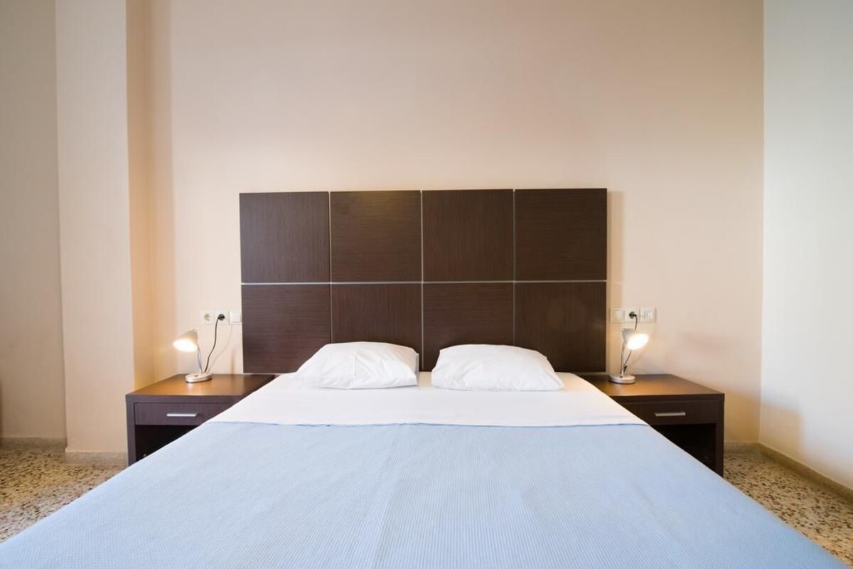 Quarto de hotel com uma cama grande, duas mesas de cabeceira e cabeceira.