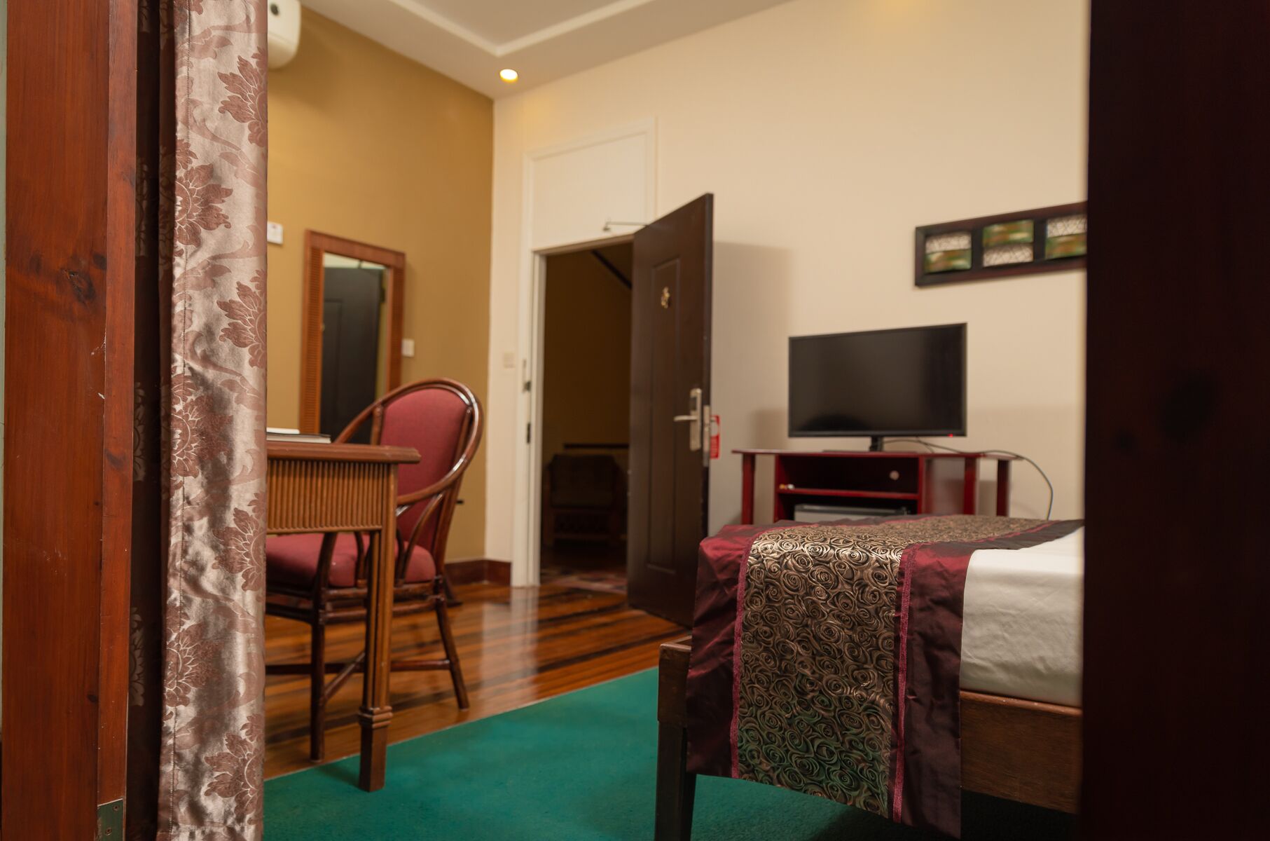Quarto de hotel com cama, escrivaninha, cadeira e televisão.
