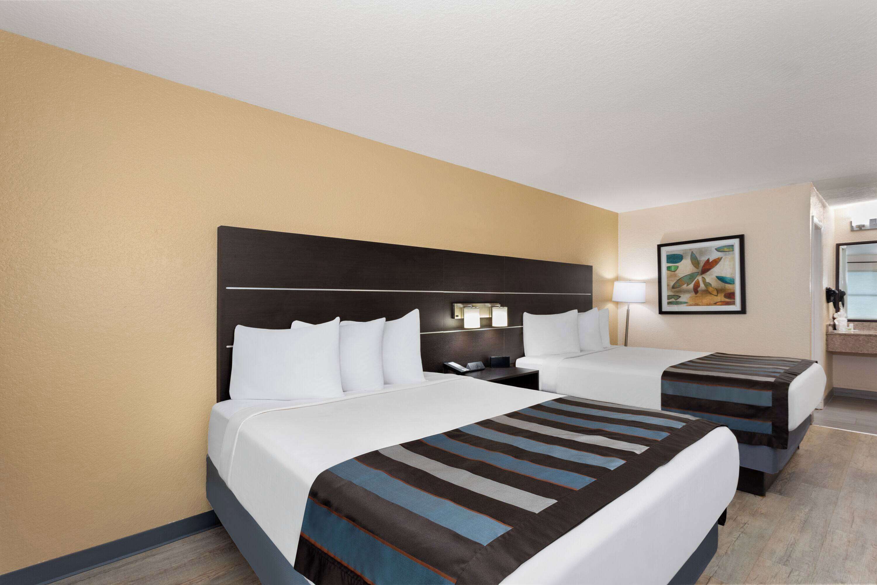 Quarto de hotel com duas camas, uma mesa de cabeceira, uma luminária e um quadro na parede.