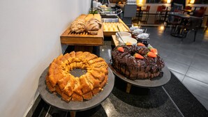Buffet com diversos pães e sobremesas, incluindo um bolo bundt e um bolo de chocolate com morangos.