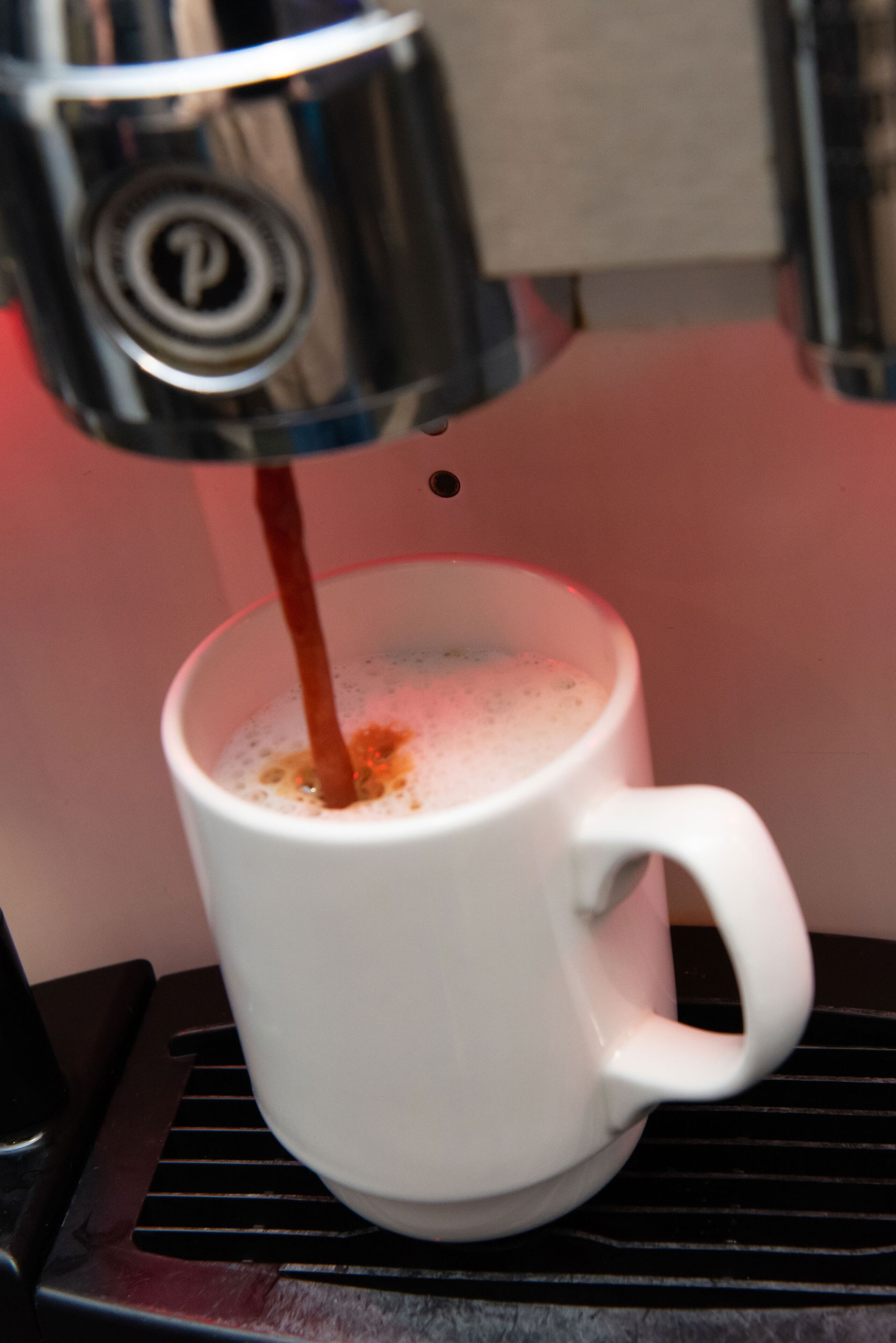 Uma chávena branca sobre um tabuleiro preto, com uma máquina de café a servir café.