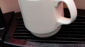 Uma chávena branca sobre um tabuleiro preto, com uma máquina de café a servir café.