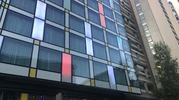 Um edifício moderno com uma fachada em grade de janelas, algumas com painéis coloridos, e uma entrada visível com portas de vidro.