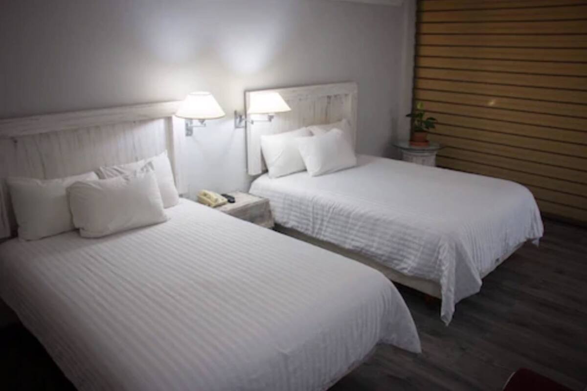 Quarto de hotel com duas camas de solteiro, cada uma com cabeceira, abajures e uma pequena mesa com telefone.