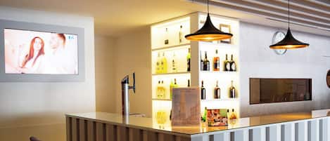 Uma área de bar com balcão, banquetas, tela de televisão e um display de vinhos.