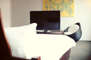 Quarto de hotel moderno com uma cama, televisão de tela plana, uma cadeira e um objeto decorativo na parede.