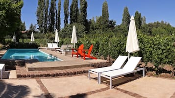 Uma área de piscina com espreguiçadeiras e guarda-sóis, rodeada por vegetação e árvores.