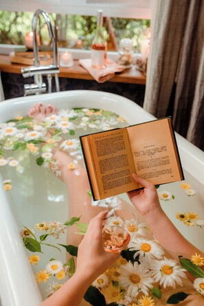 Uma banheira cheia de água e flores, com um livro segurado por alguém.