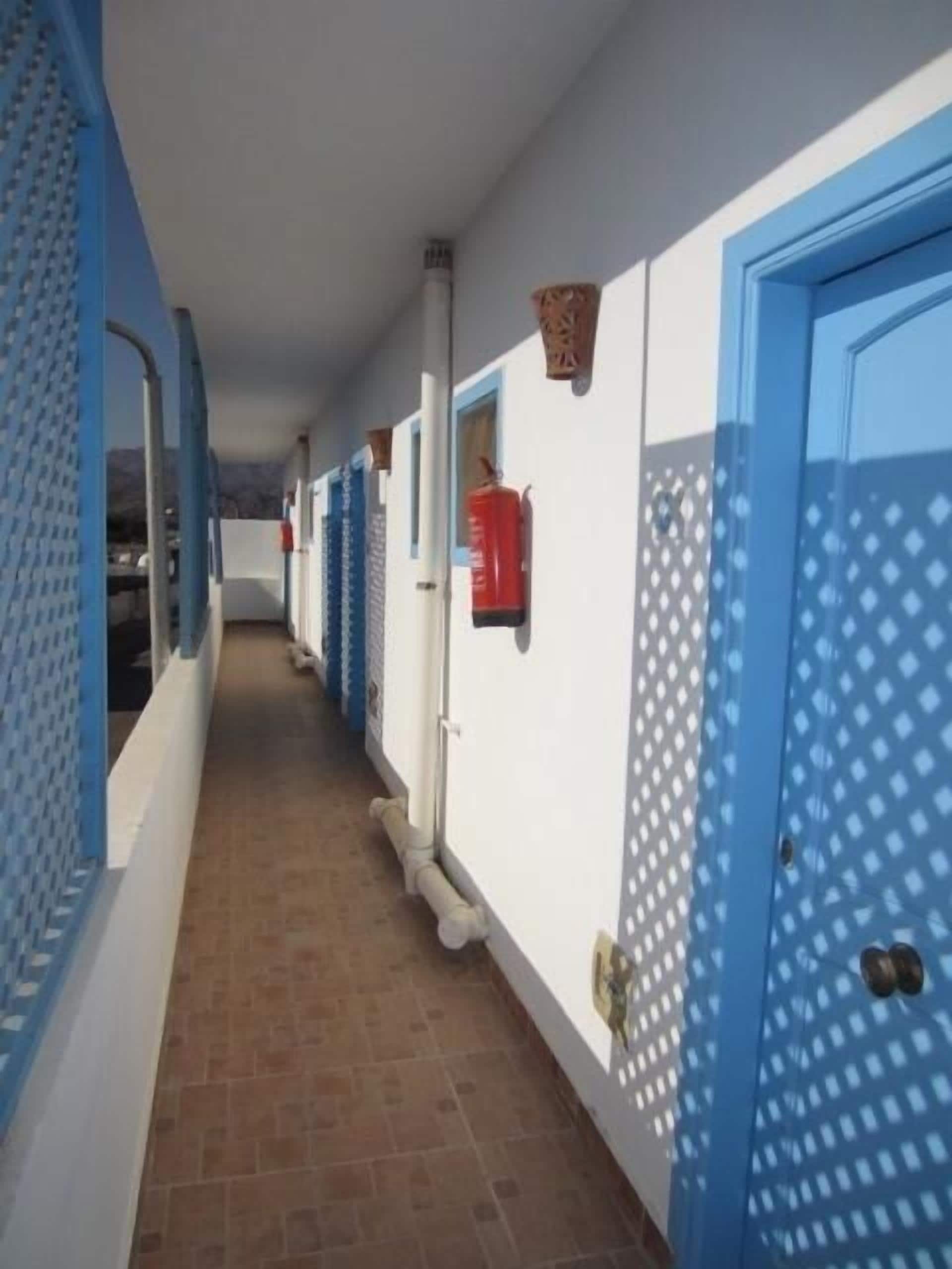 Um corredor com portas azuis, um extintor de incêndio e chão de azulejos.