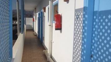 Um corredor com portas azuis, um extintor de incêndio e chão de azulejos.