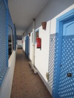 Um corredor com portas azuis, um extintor de incêndio e chão de azulejos.