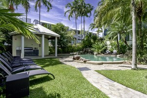 Área da piscina com espreguiçadeiras, um espaço de estar coberto e uma pequena cascata.
