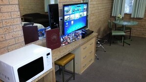 Quarto com televisão, micro-ondas, uma mesa pequena e uma cadeira.