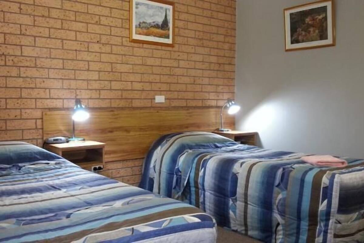 Quarto com duas camas, cada uma com roupa de cama listrada, cabeceiras de madeira e luminárias laterais.