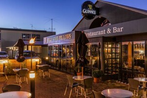 Uma área de estar ao ar livre com mesas e cadeiras, um letreiro de restaurante e bar, e um letreiro da Guinness.