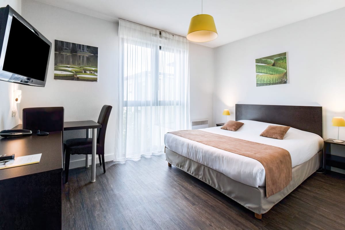 Quarto de hotel com cama, escrivaninha, cadeira, televisão e obras de arte nas paredes.