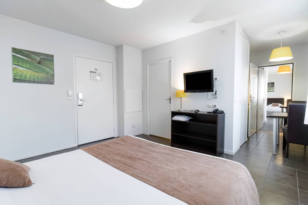 Quarto de hotel com cama, secretária, cadeira, televisão e abajur.