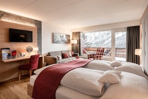 Quarto de hotel com uma cama grande, uma escrivaninha com televisão de tela plana, uma cadeira, um sofá e uma varanda com vista para árvores cobertas de neve.