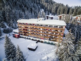 Um hotel com várias andares e telhado coberto de neve, rodeado por uma floresta.