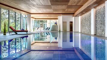Piscina interna com paredes de vidro transparente, teto de madeira e uma cadeira de descanso vermelha.