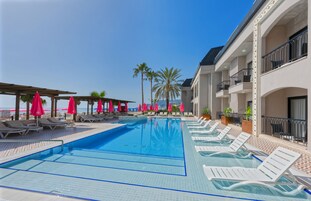 Uma área de piscina com espreguiçadeiras e guarda-sóis, um edifício com varandas e palmeiras.