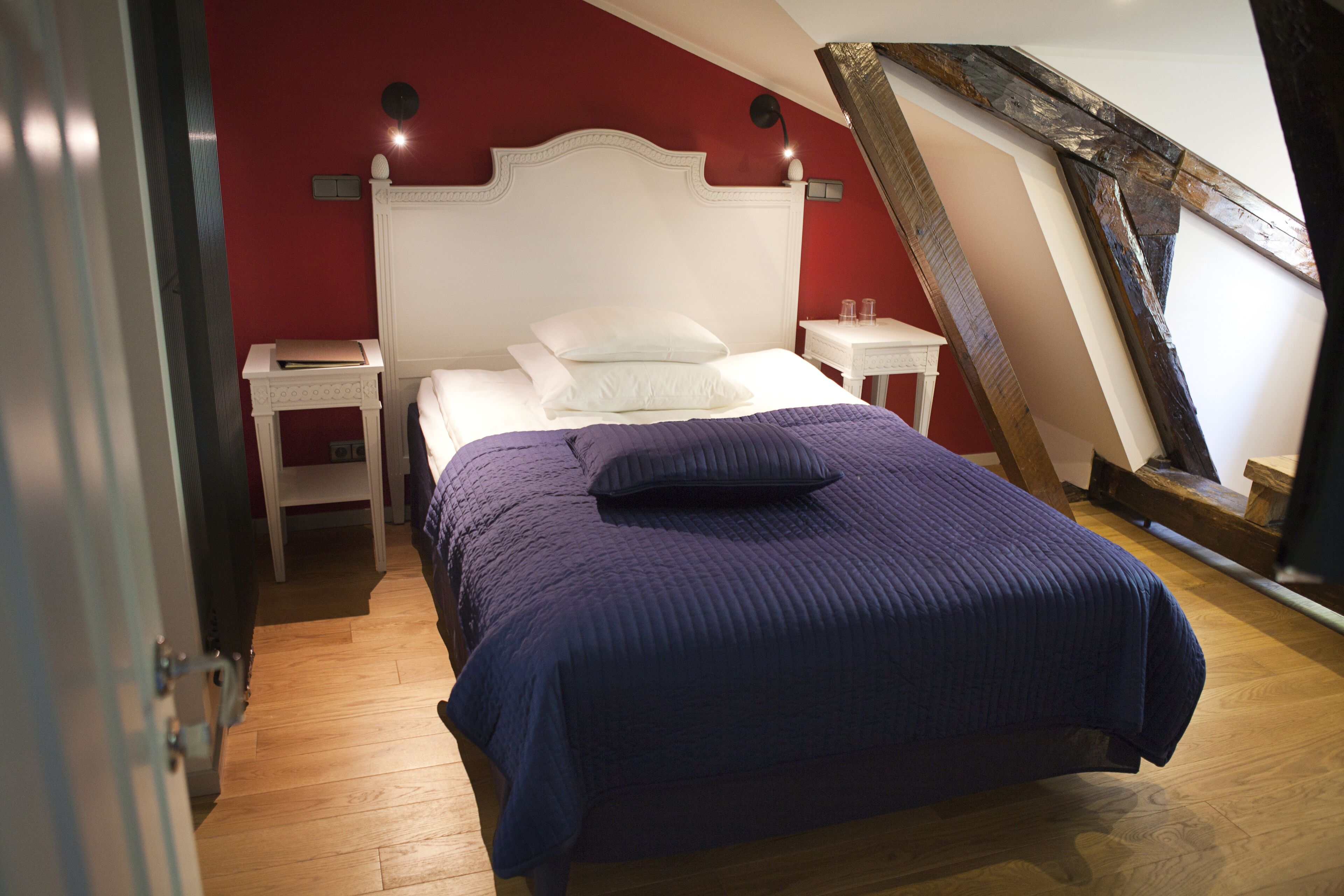 Quarto com cabeceira branca, piso de madeira e teto inclinado.
