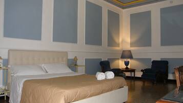Quarto de hotel com uma cama grande, duas cadeiras, uma mesa e um abajur.